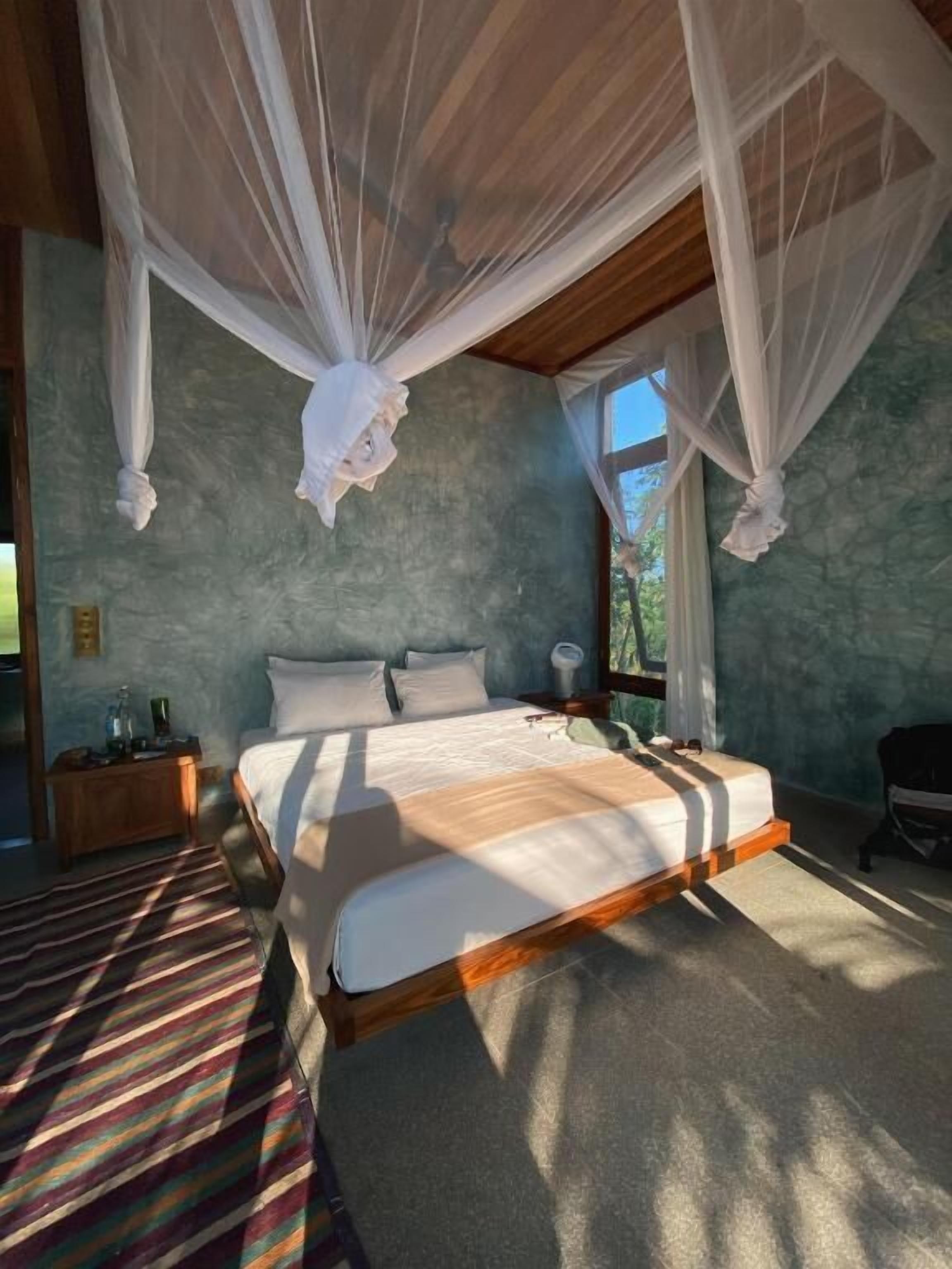 Quarto com cama, mesa de cabeceira e janela com cortinas.