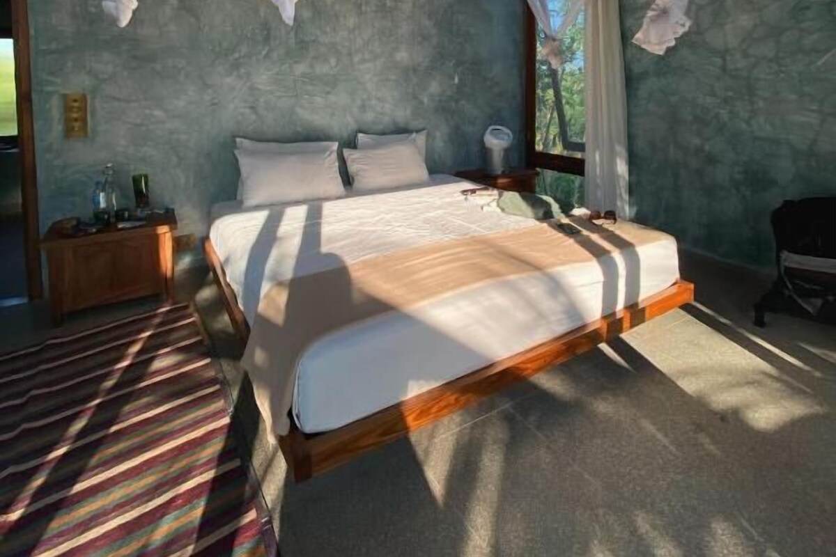 Quarto com cama, mesa de cabeceira e janela com cortinas.