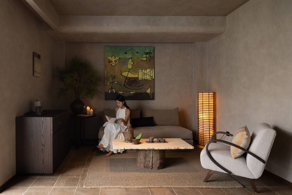 Um quarto aconchegante com uma cama, uma poltrona, uma mesa de centro e um quadro na parede.