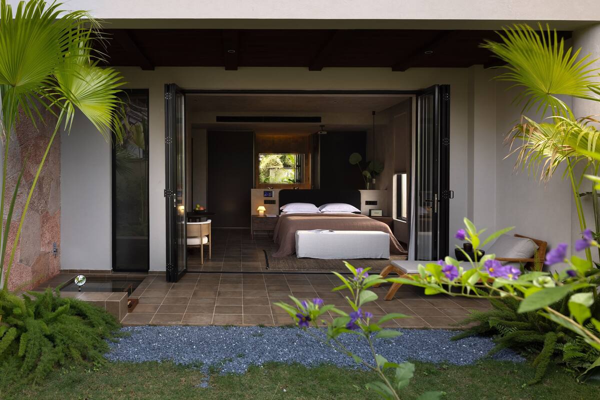 Quarto com uma cama grande, uma mesa de cabeceira e um criado-mudo. Há uma janela com vista para o verde lá fora.