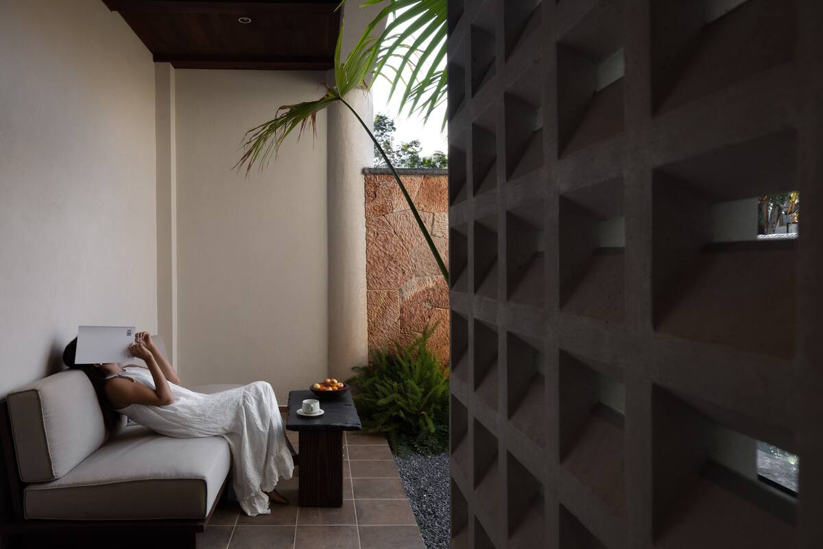 Uma pessoa deitada num sofá numa sala com chão em azulejos, uma mesinha com uma tigela de fruta e uma planta.