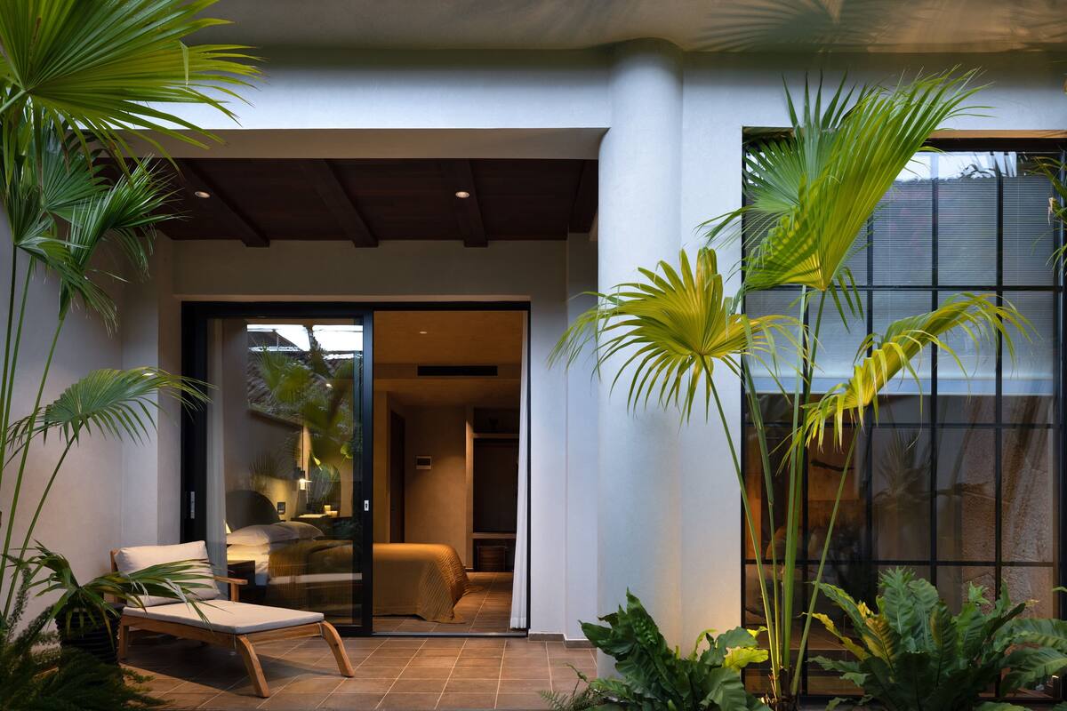 Um interior moderno com uma porta de vidro que dá para um quarto, cercado por plantas e uma poltrona de descanso.