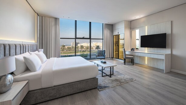 Quarto de hotel moderno com uma cama grande, uma escrivaninha, uma TV e vista para a cidade.