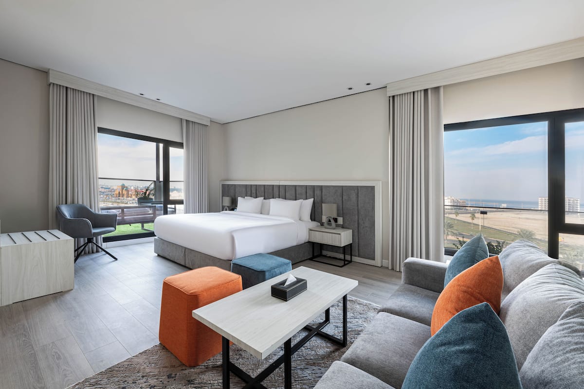 Quarto de hotel moderno com uma cama grande, um sofá, uma mesa de centro e vista para a cidade.