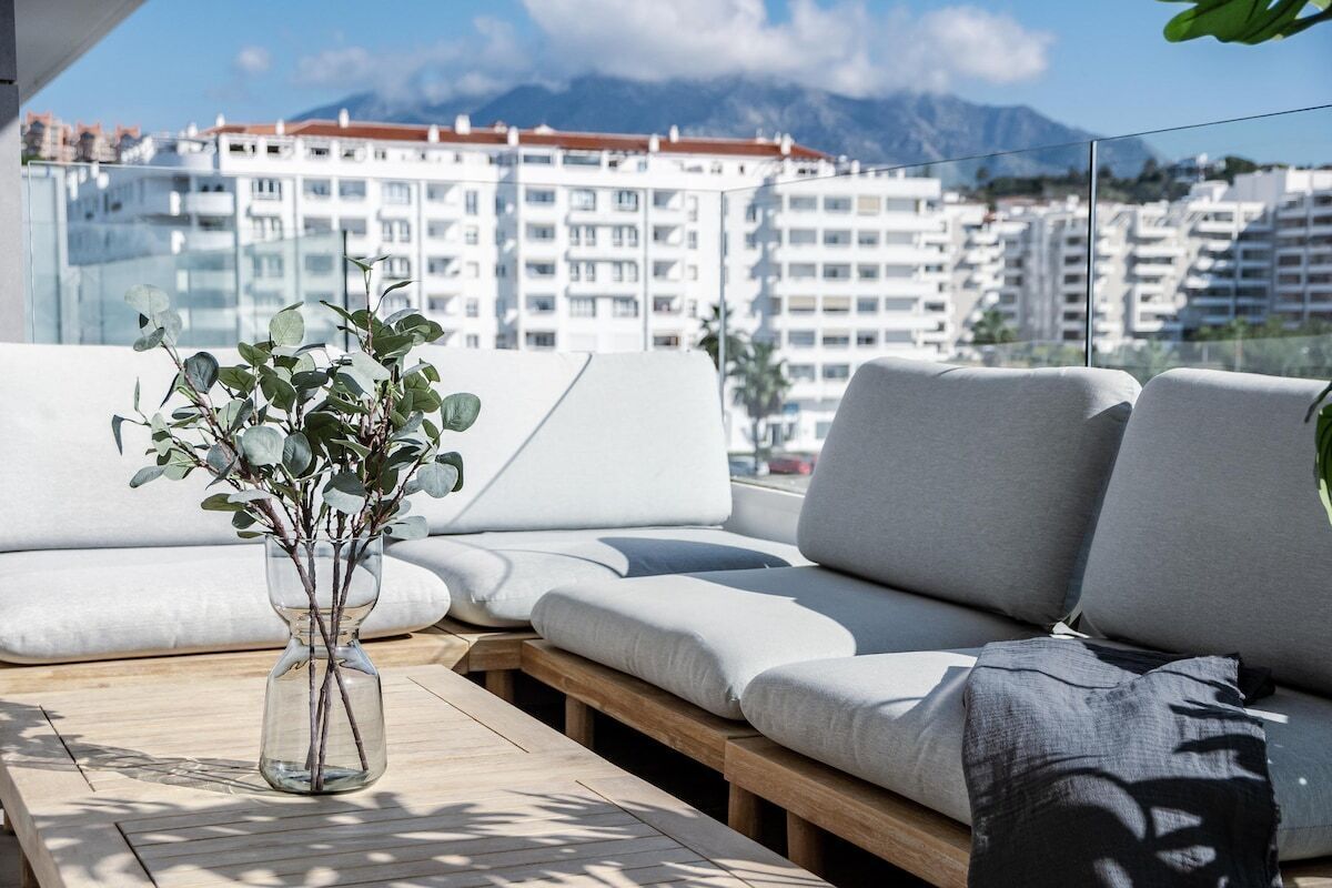 Uma área de estar moderna ao ar livre, com vista clara para um horizonte urbano e montanhas ao fundo.