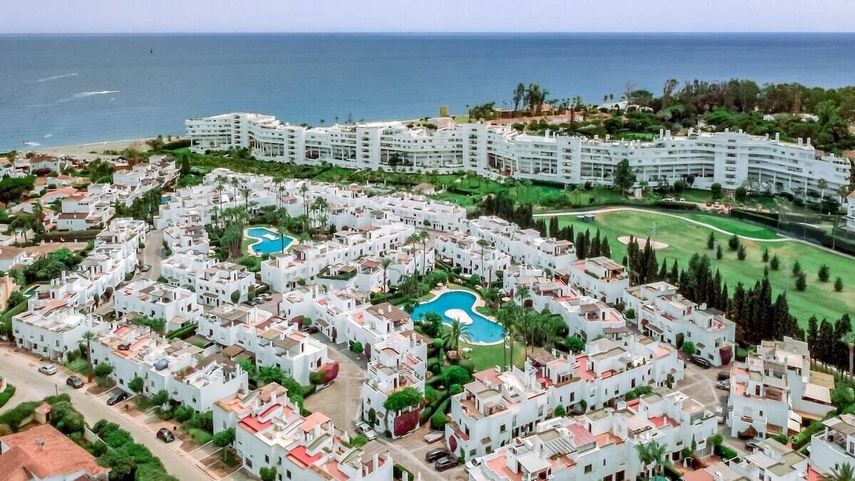 Resort com vários edifícios brancos, uma piscina central e vista para o oceano.