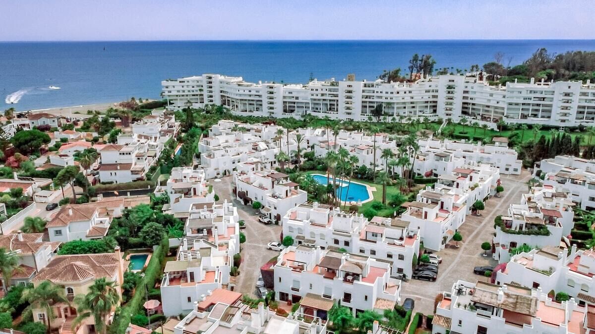 Uma área residencial costeira com edifícios brancos, piscina central e vista para o mar.