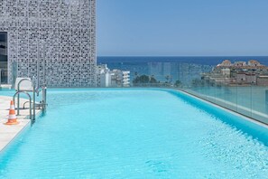 Piscina infinita no terraço, com vista clara do oceano e edifícios à beira-mar.