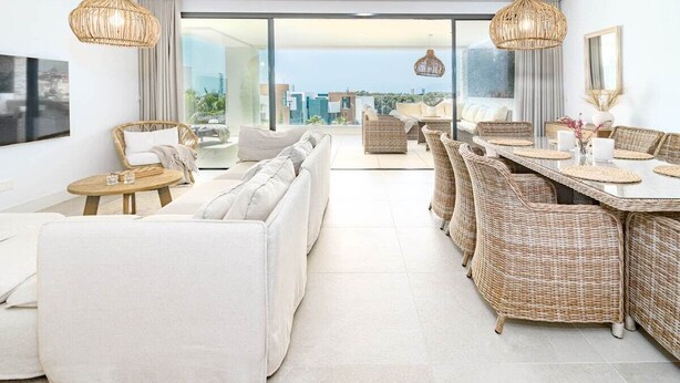 Uma sala de estar espaçosa com um sofá grande, mesa de jantar e móveis de vime.
