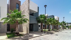 Um edifício moderno com fachada de pedra, um telhado plano e um pátio pavimentado com palmeiras.