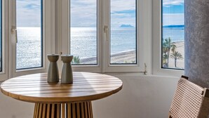 Quarto com uma mesa redonda de madeira e dois saleiros, uma cadeira de vime e vista para o mar por grandes janelas.