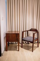Uma cadeira de madeira e uma mesa de madeira combinando numa divisão com cortinas claras e soalho de madeira.