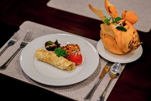 Um prato com um rolo de omelete, peito de frango grelhado e tomate grelhado, acompanhado por um pão com cobertura decorativa.