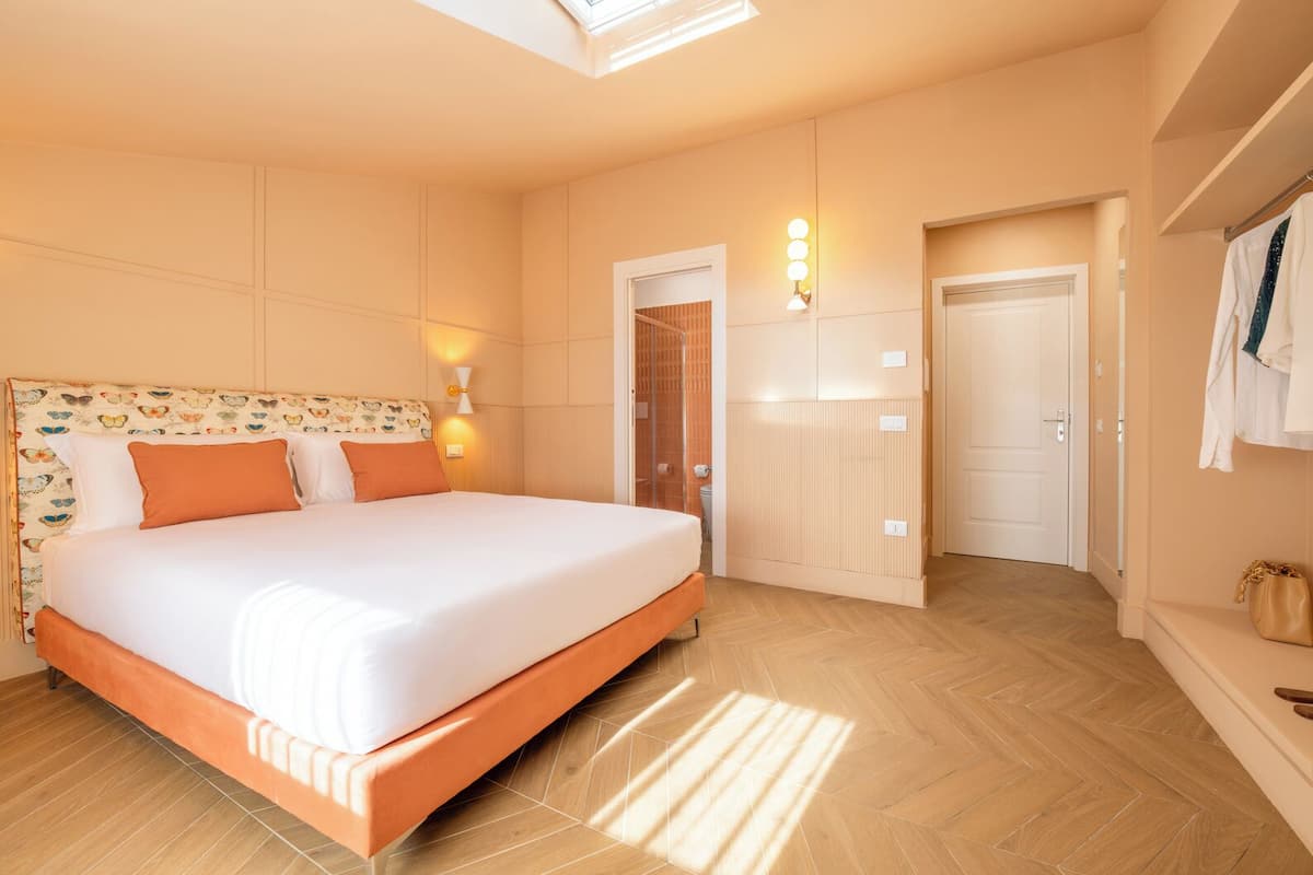 Quarto com cama, mesa de cabeceira, luminária na parede e porta para outro espaço.