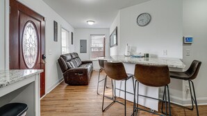 Cozinha moderna com bancada de mármore, espaço de bar embutido com banquetas, sofá de couro e uma janela grande com persianas.