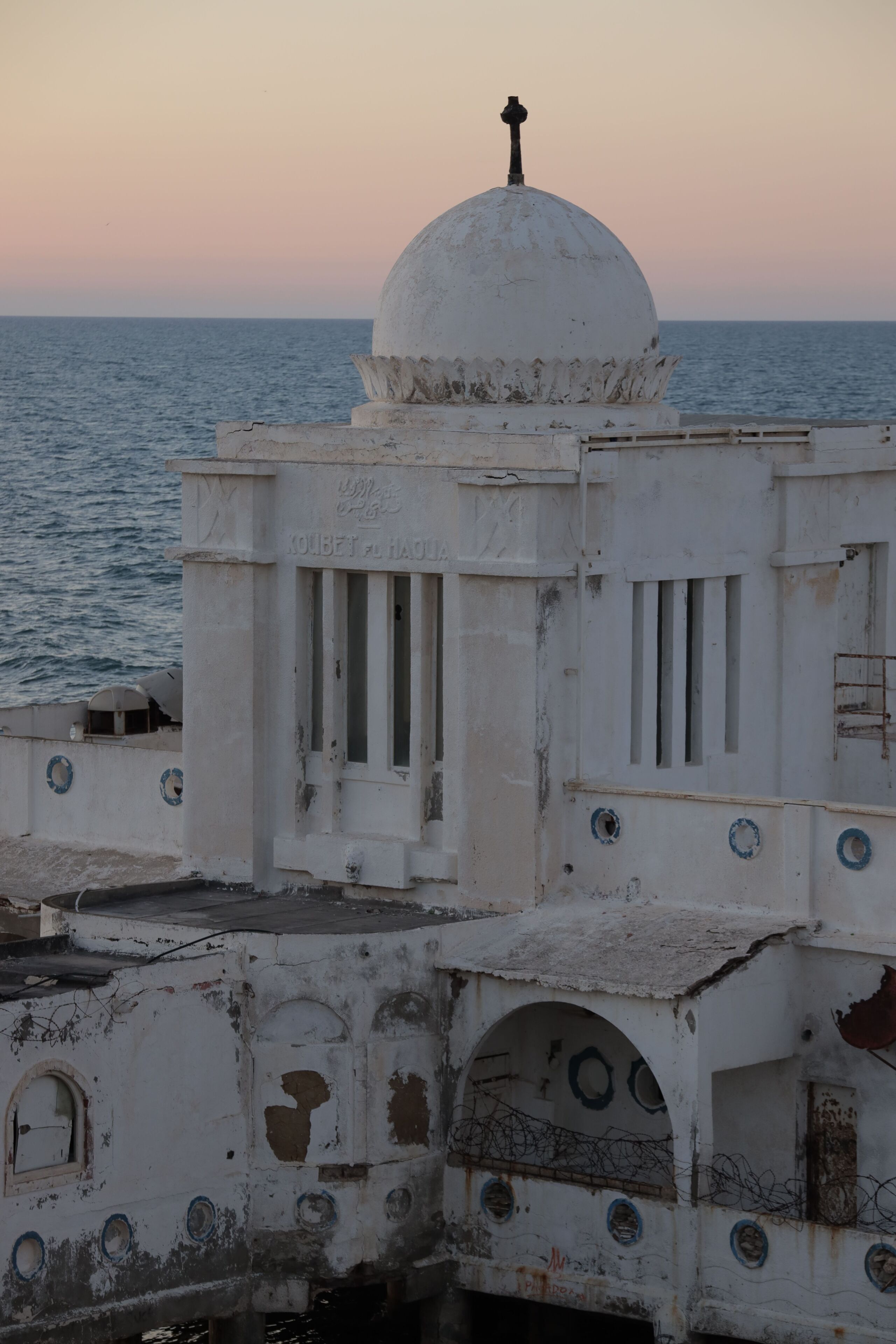 Um edifício branco com uma cúpula e uma cruz no topo, perto de um corpo d'água.