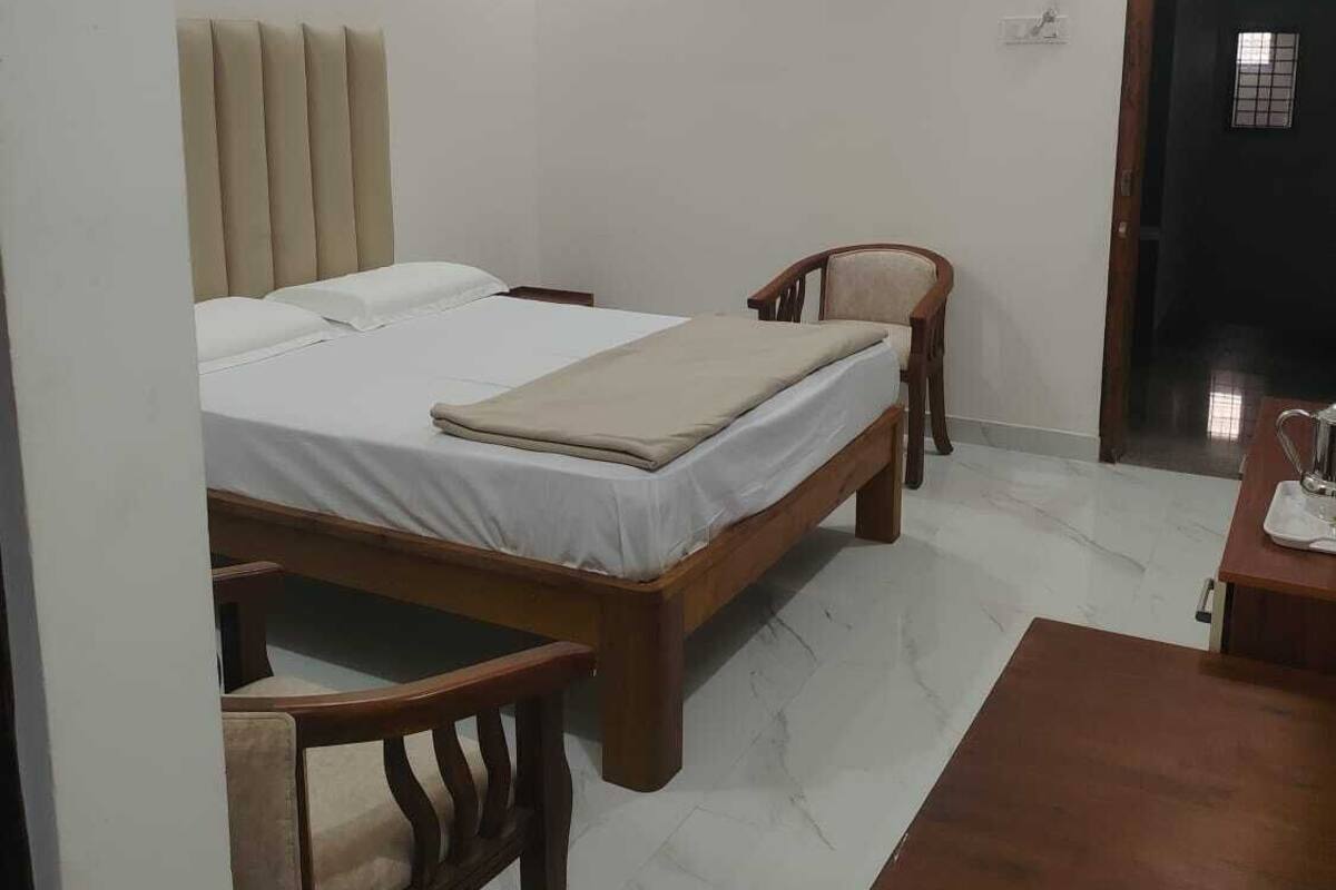Quarto com uma cama, duas cadeiras, uma mesa, um ventilador de teto e uma porta.