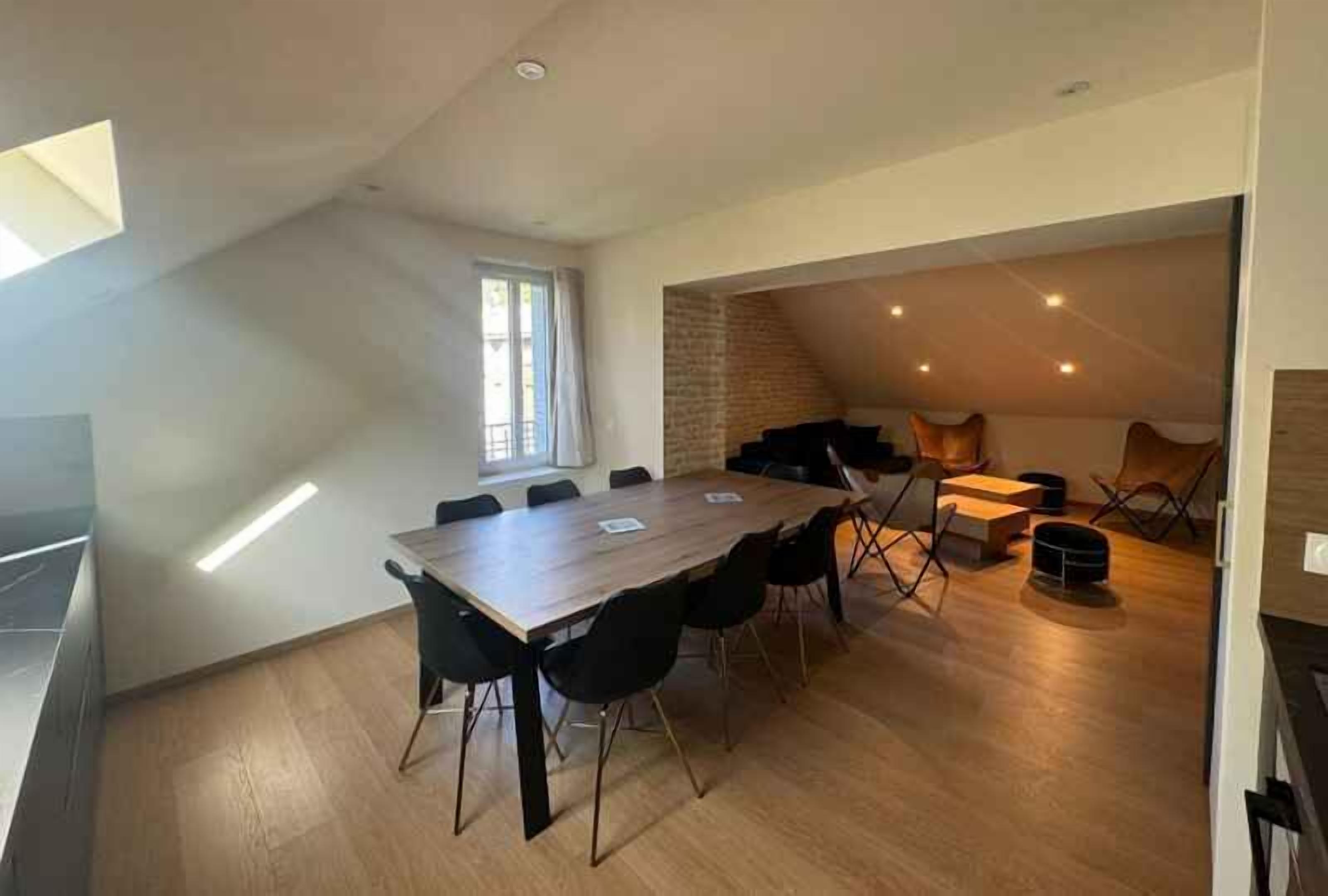 Um quarto amplo com uma grande mesa de madeira, cadeiras pretas e uma parede de tijolos.