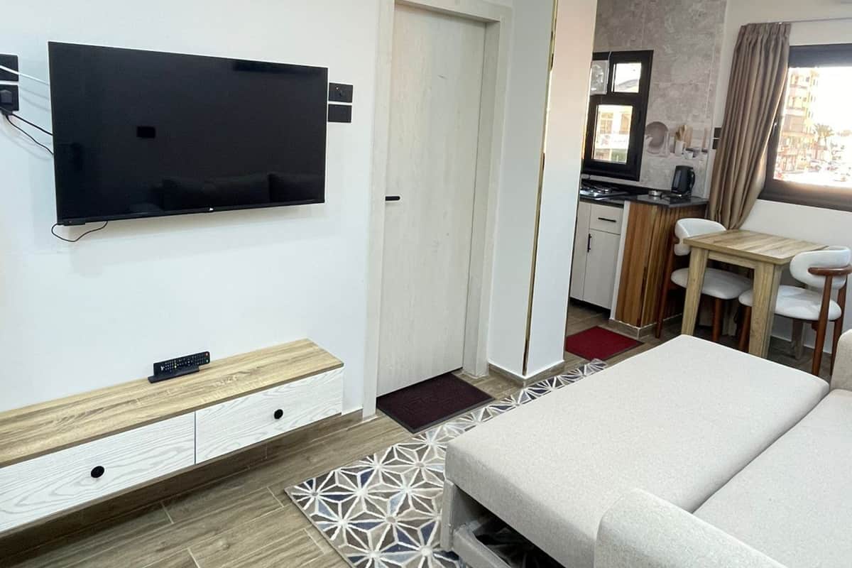 Uma sala de estar moderna com uma televisão de tela plana, um sofá, uma mesa de centro de madeira e um tapete estampado.