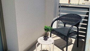 Uma pequena varanda com espaço ao ar livre, uma cadeira, uma mesinha e um vaso de planta.