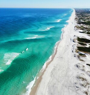 Vista aérea de uma praia com águas turquesas cristalinas e uma faixa de areia.