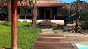 Uma trilha de madeira leva a um edifício com telhado vermelho e estruturas com telhado de palha.