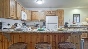 Uma cozinha com armários de madeira, geladeira branca, bancada de granito e três banquetas.