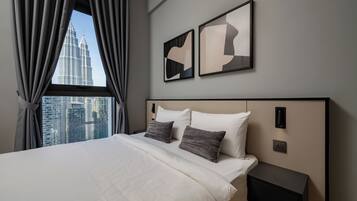Quarto de hotel com uma cama grande, duas almofadas, uma mesa de cabeceira e uma janela com vista para a paisagem urbana.