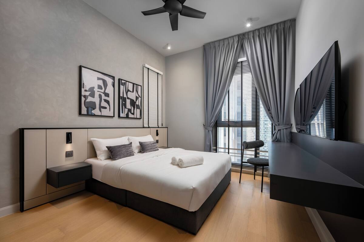 Quarto moderno com cama, mesas de cabeceira, obras de arte, ventilador de teto, janela com cortinas e TV.