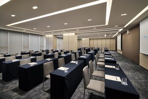 Uma sala de conferências com mesas, cadeiras dispostas em fileiras e uma tela de projeção.