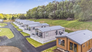 Uma fileira de casas móveis modernas com varandas integradas, situada numa área ajardinada com uma floresta ao fundo.