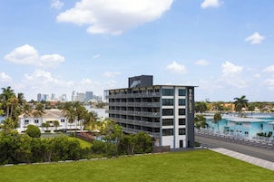 Um hotel moderno de vários andares com área de piscina, rodeado por vegetação e com o horizonte da cidade ao fundo.