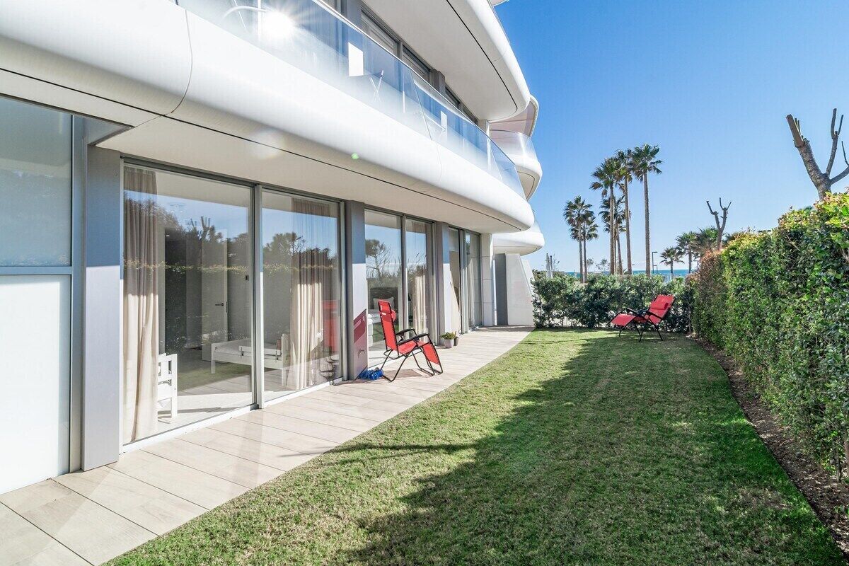 Uma casa moderna com grandes portas de vidro, um pátio com cadeiras vermelhas e um jardim bem cuidado.