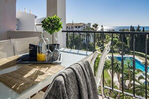 Varanda com mesa posta para o café da manhã, planta em vaso e vista para uma piscina e o oceano.