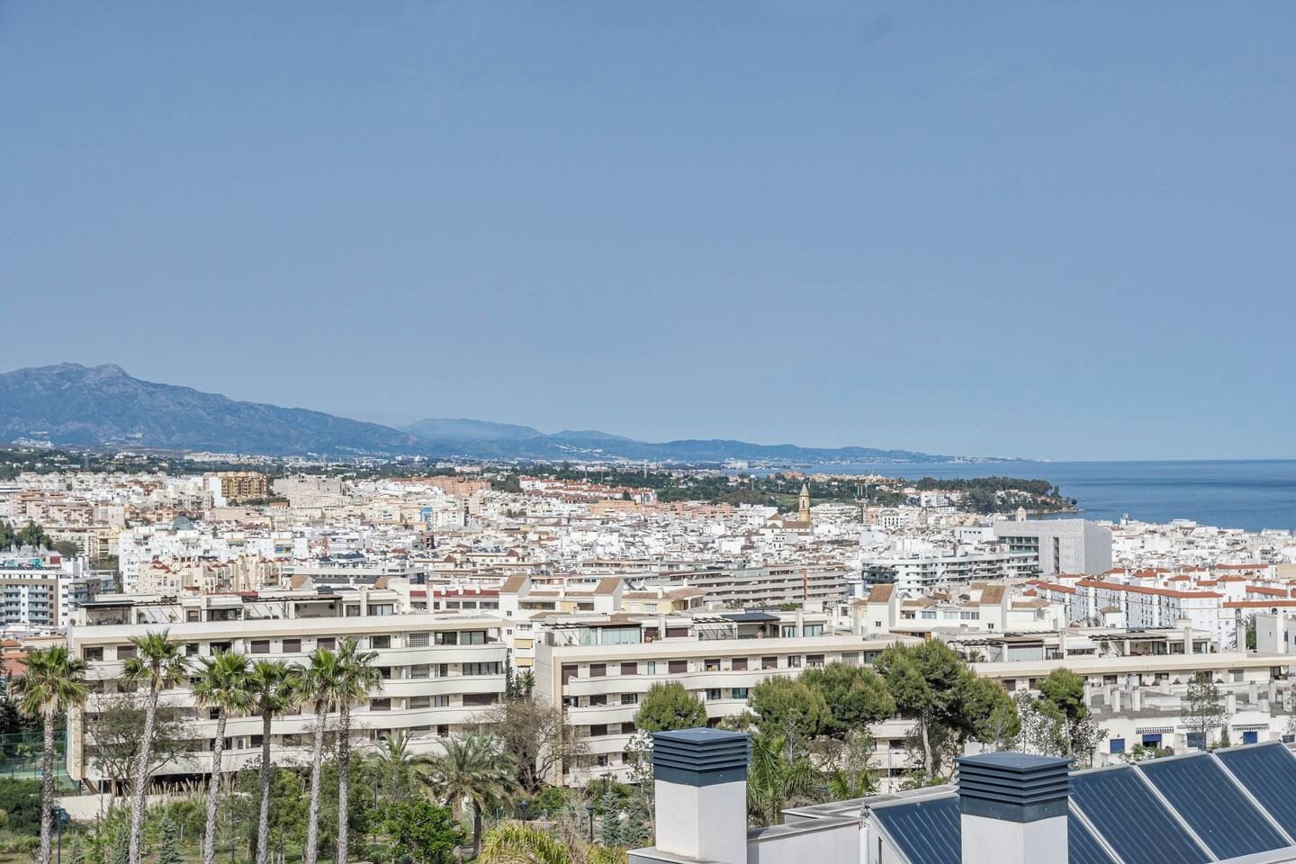 Paisagem costeira urbana com vista para o mar e montanhas ao longe.