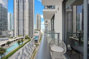 Varanda com vista para edifícios altos, piscina e uma cadeira.