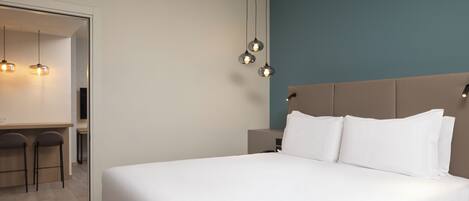 Quarto de hotel moderno com uma cama grande, uma escrivaninha com duas cadeiras e iluminação pendente.