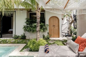 Área da piscina com porta de madeira, parede branca e um espaço coberto com assentos e uma toalha.