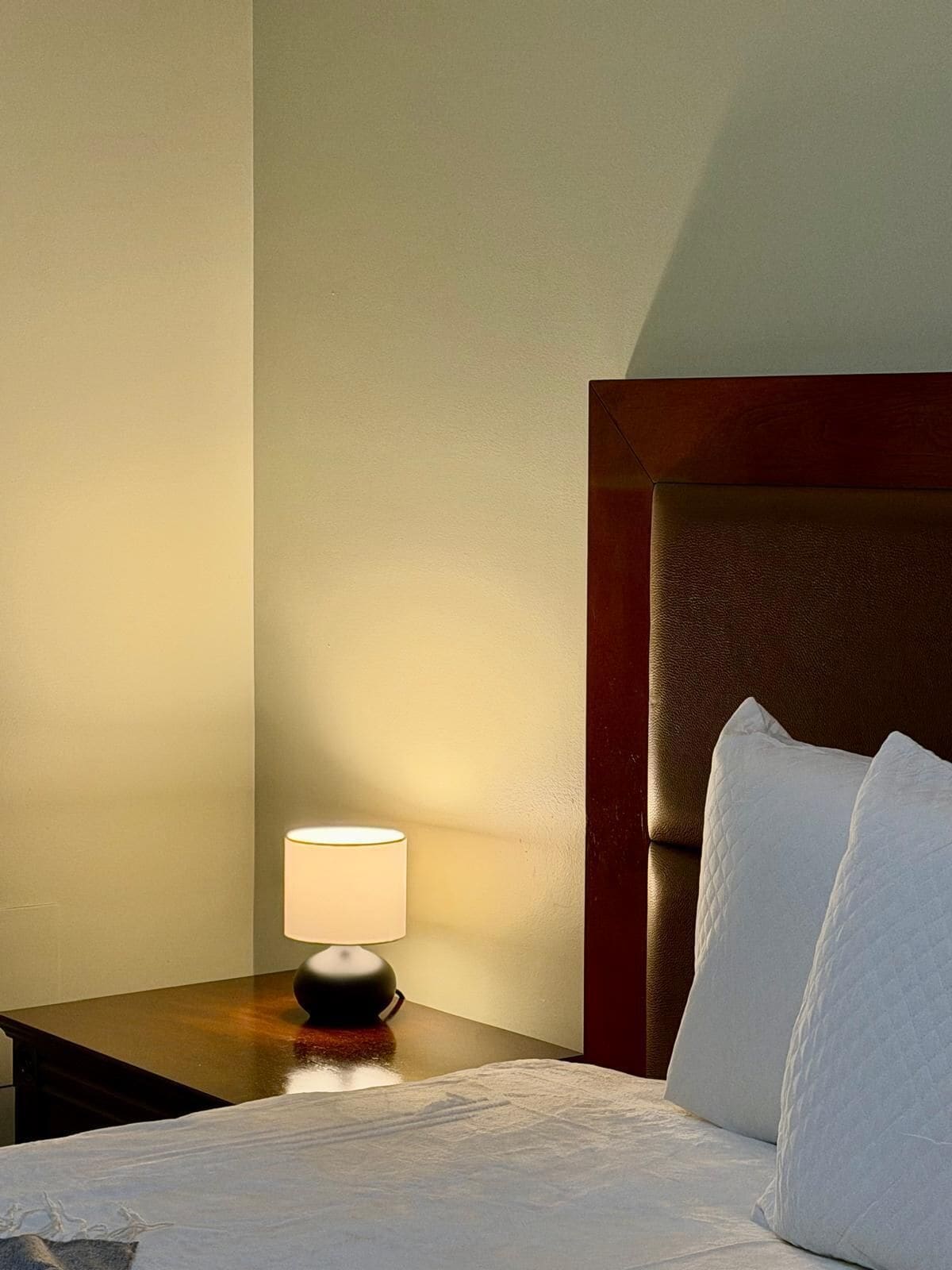 Quarto de hotel com uma cama bem arrumada, abajur e cabeceira de madeira.