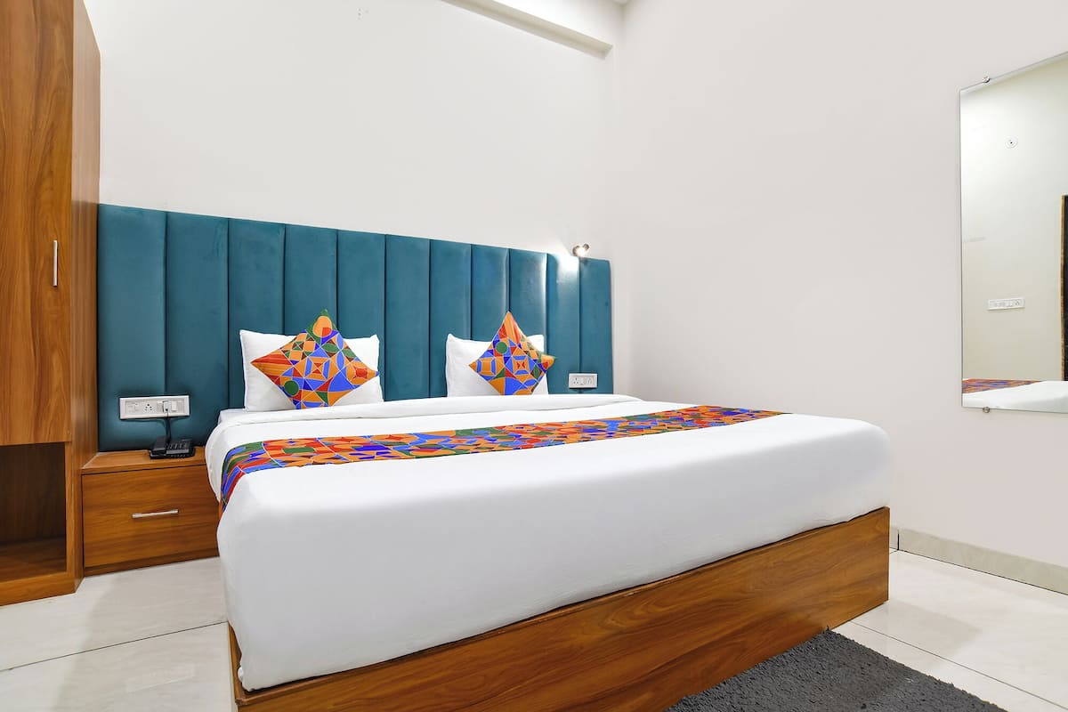 Quarto moderno com cabeceira de madeira, colcha branca e dois travesseiros com padrão geométrico.