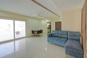 Uma sala de estar ampla com um sofá azul, uma mesa de jantar com cadeiras e uma grande porta de vidro deslizante que dá para uma área externa.
