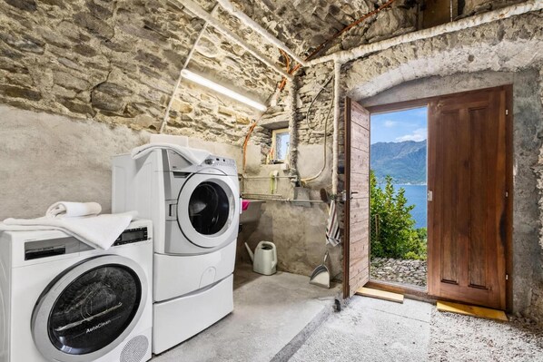 Uma lavanderia com duas máquinas de lavar, uma porta de madeira que dá para o exterior e vista para montanhas pela porta.