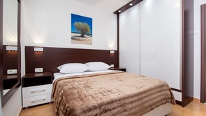 Quarto com cama, mesa de cabeceira, cómoda, um quadro de uma árvore e guarda-roupa.