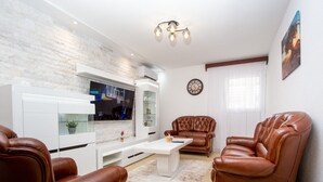 Uma sala de estar moderna com sofás de couro, uma mesa de centro branca, uma televisão de tela plana e uma parede de destaque em pedra.