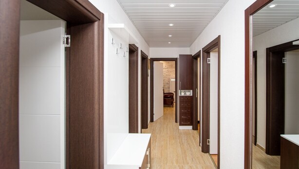 Um corredor com portas de madeira, paredes brancas e chão em azulejos.