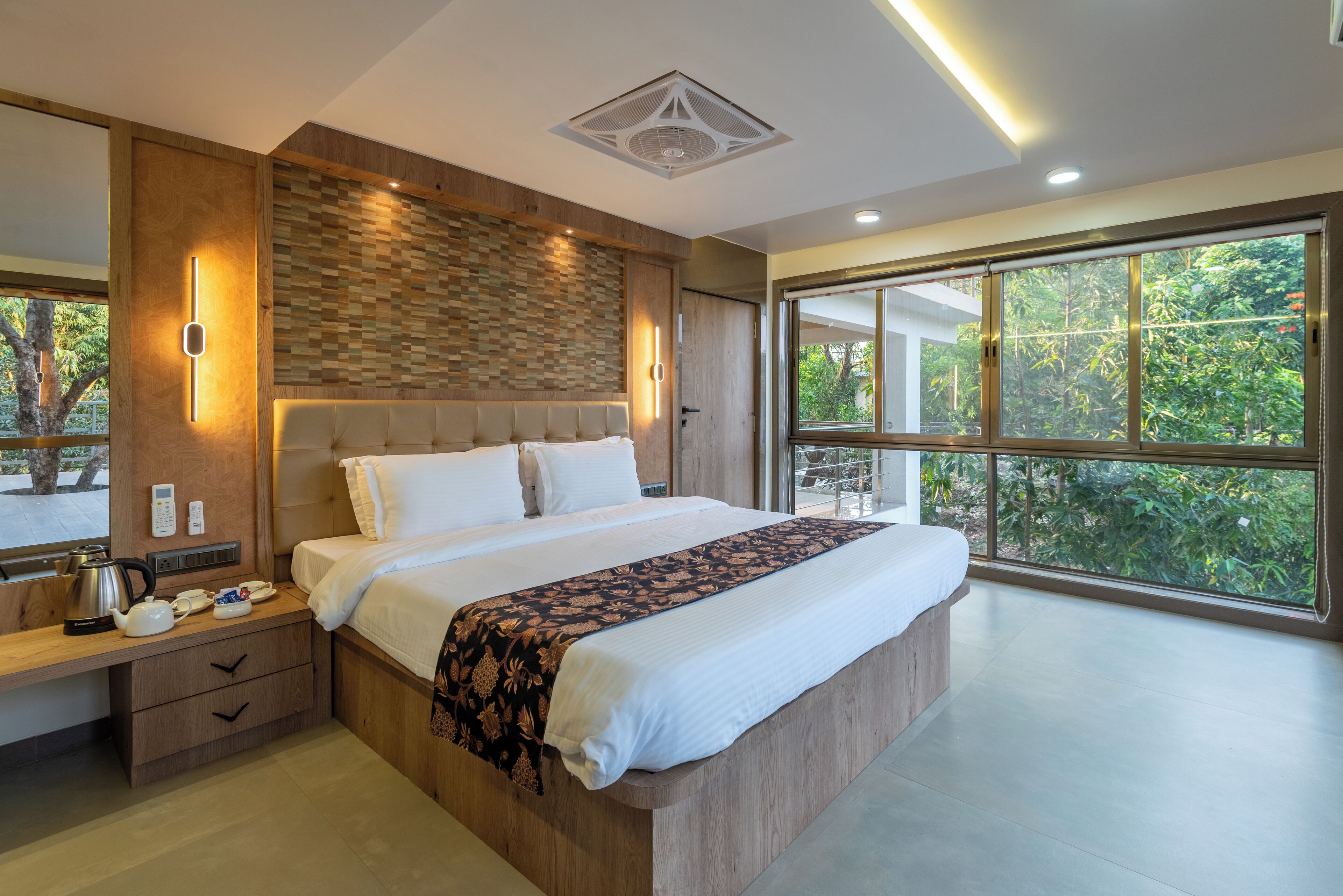 Quarto moderno com uma cama grande, cabeceira de madeira, mesas de cabeceira e uma janela ampla com vista para o verde.