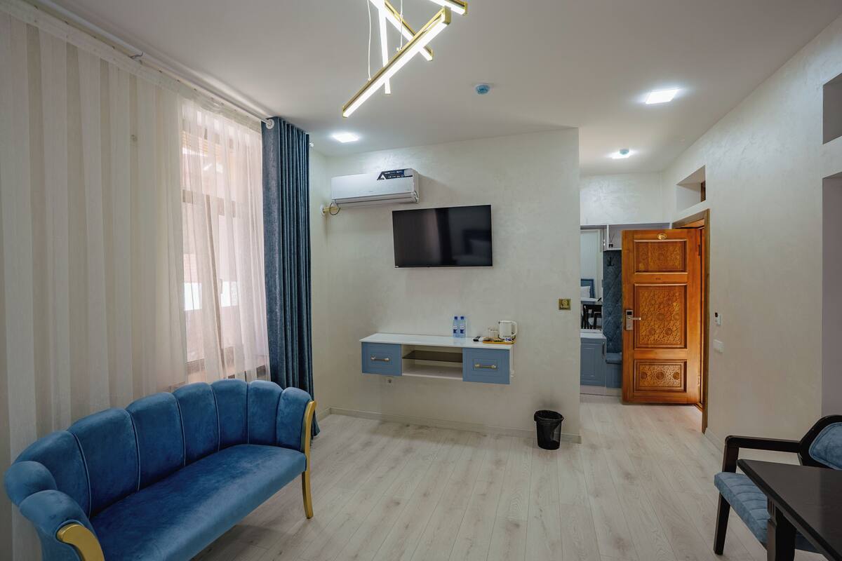 Uma sala de estar com sofá, televisão fixada na parede, mesinha e porta de madeira que dá para a cozinha.