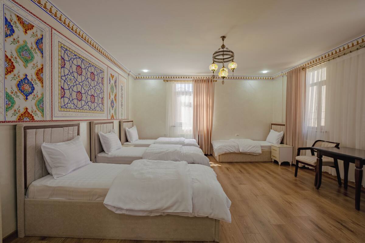 Quarto de hotel com quatro camas, um candelabro, piso de madeira e uma mesa de jantar.
