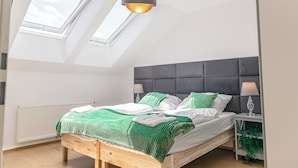 Quarto com teto inclinado, claraboias, cama com roupa de cama verde, duas luminárias de cabeceira e um radiador branco.