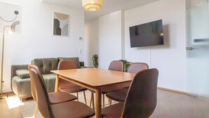 Uma sala de estar moderna com uma mesa de jantar de madeira, sofá de couro e uma TV de tela plana na parede.